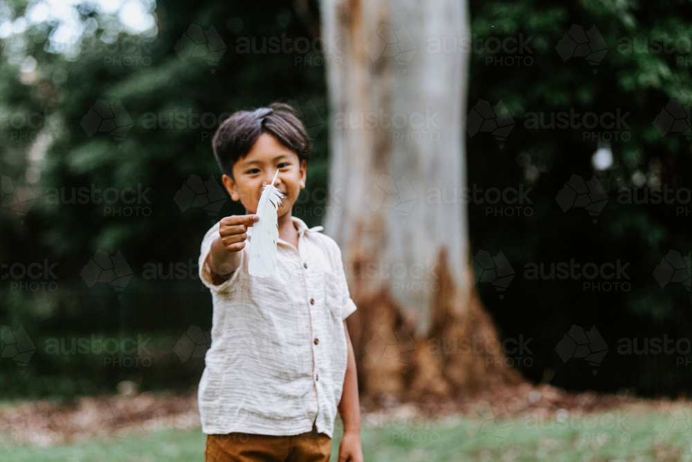 Image of Young boy holding out a white birds feather - Austockphoto