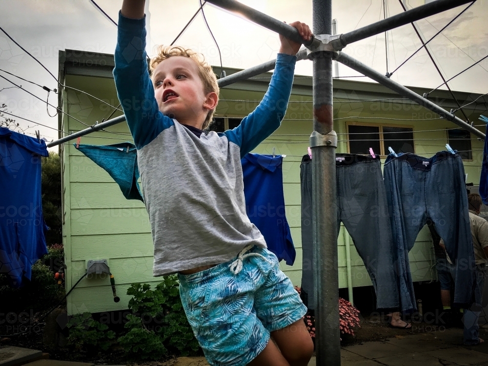 Image of Young boy playing on hills hoist in front of weatherboard ...