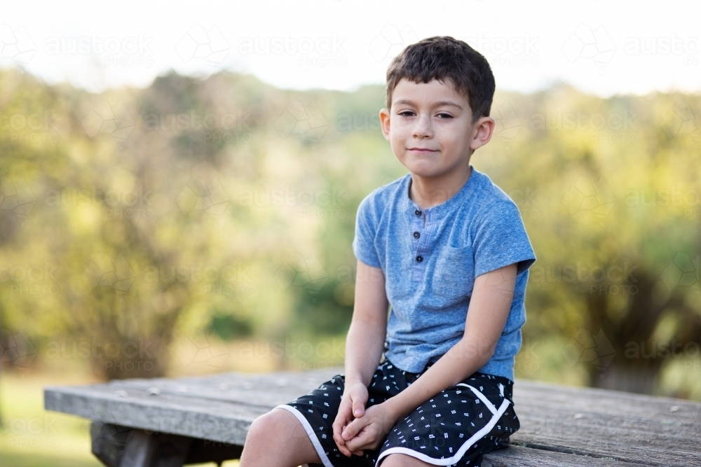 Image of Young boy sitting on bench smiling - Austockphoto
