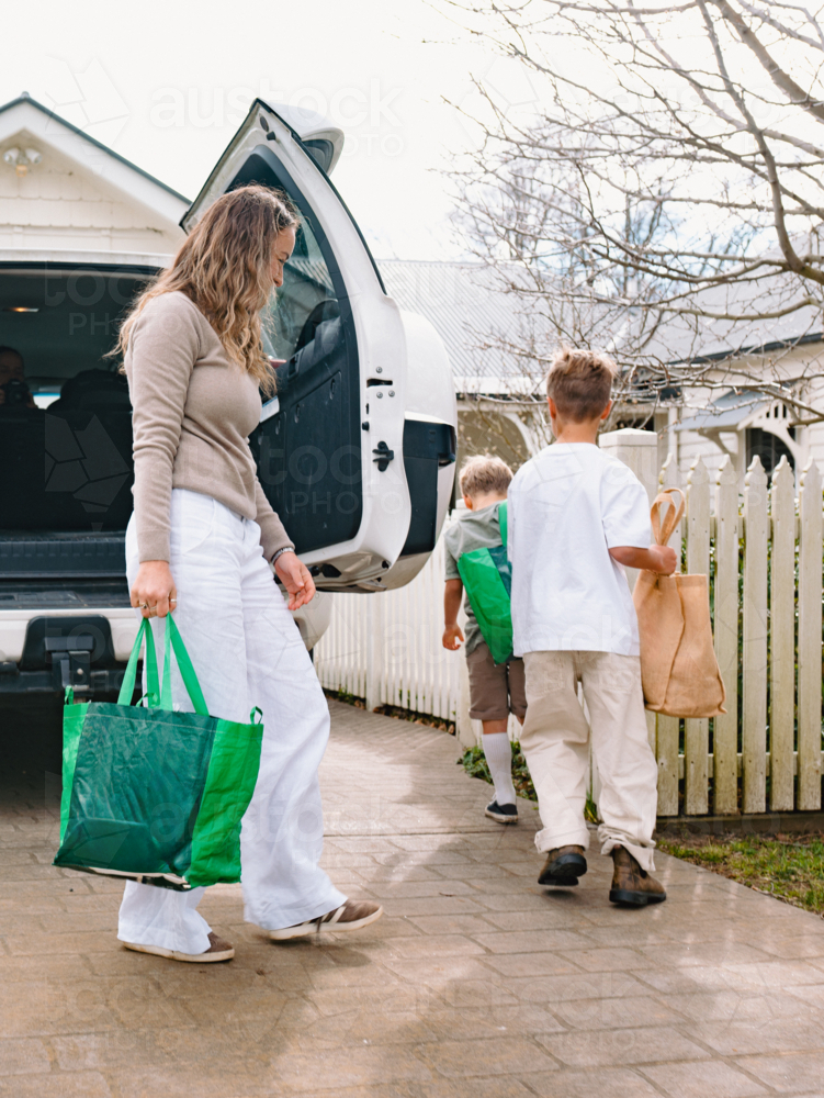 Image of Young boys helping mum carry grocery bags from car boot to the ...