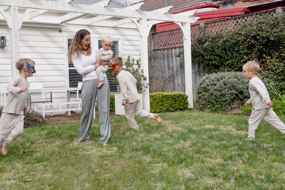 Image of Young boys running around mum holding a baby in the garden ...