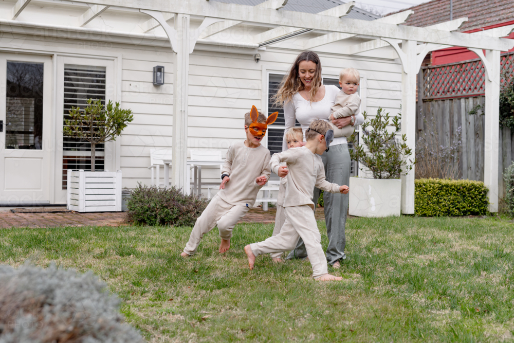 Image of Young boys running around mum holding a baby in the garden ...