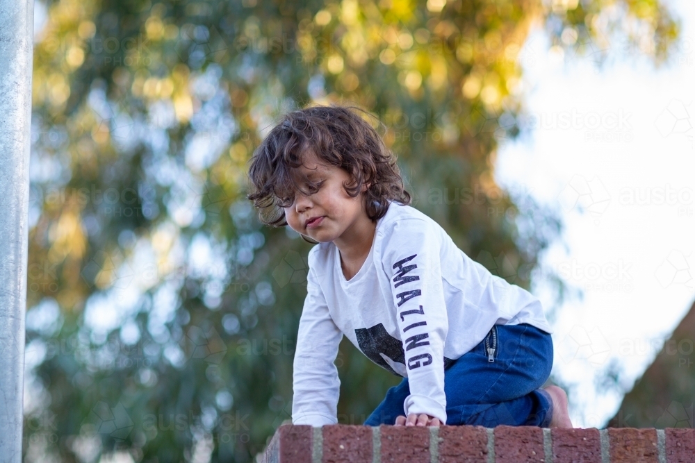 Image of Young child looking down from brick wall - Austockphoto