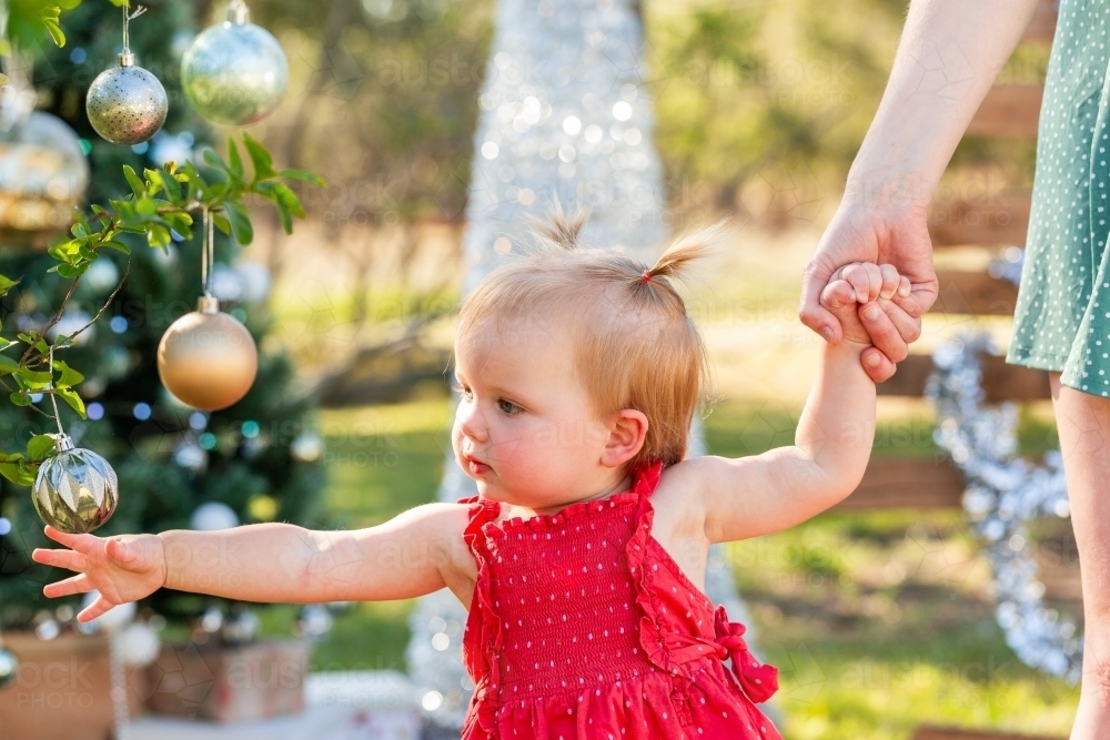 Image of Young child reaching out to grab bauble hanging on tree ...