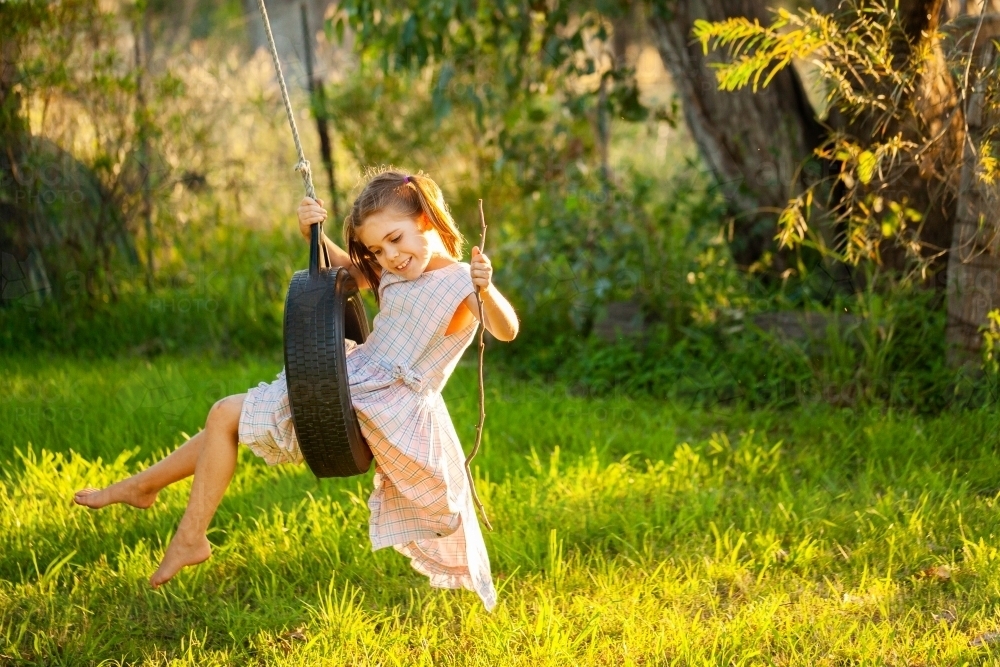 Image of Young country kid in dress swinging on tyre swing in tree ...