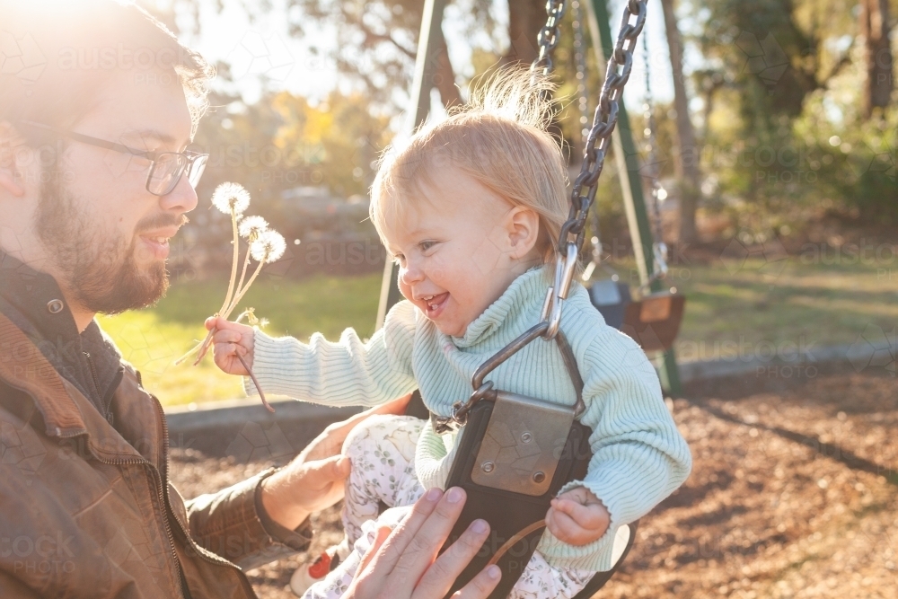 Image of Young dad pushing one year old daughter on swing in park while ...