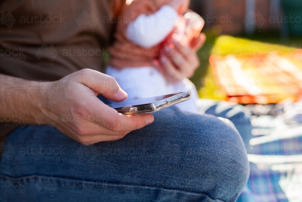 Image of Young dad using phone technology while holding baby outside ...
