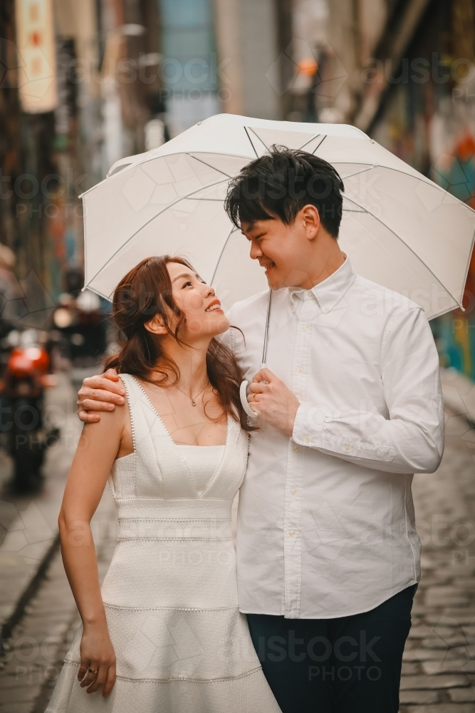 Image of Young engaged couple posing with white umbrella in Hosier Lane ...