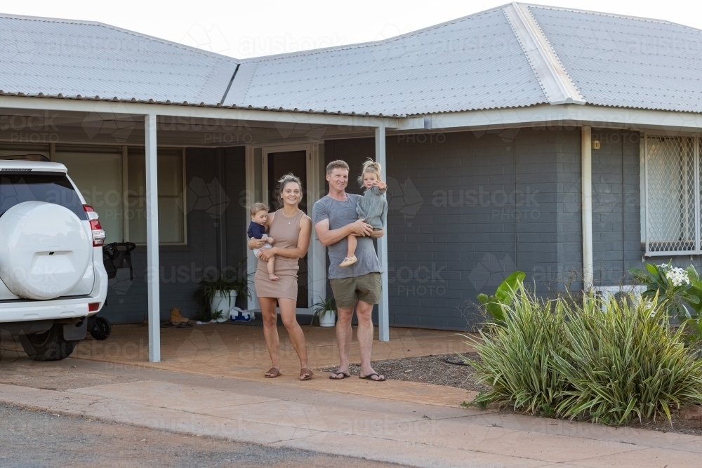Image of young family standing outside their modest home - Austockphoto