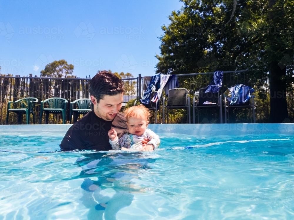 Image of Young father in pool with baby in summer - Austockphoto