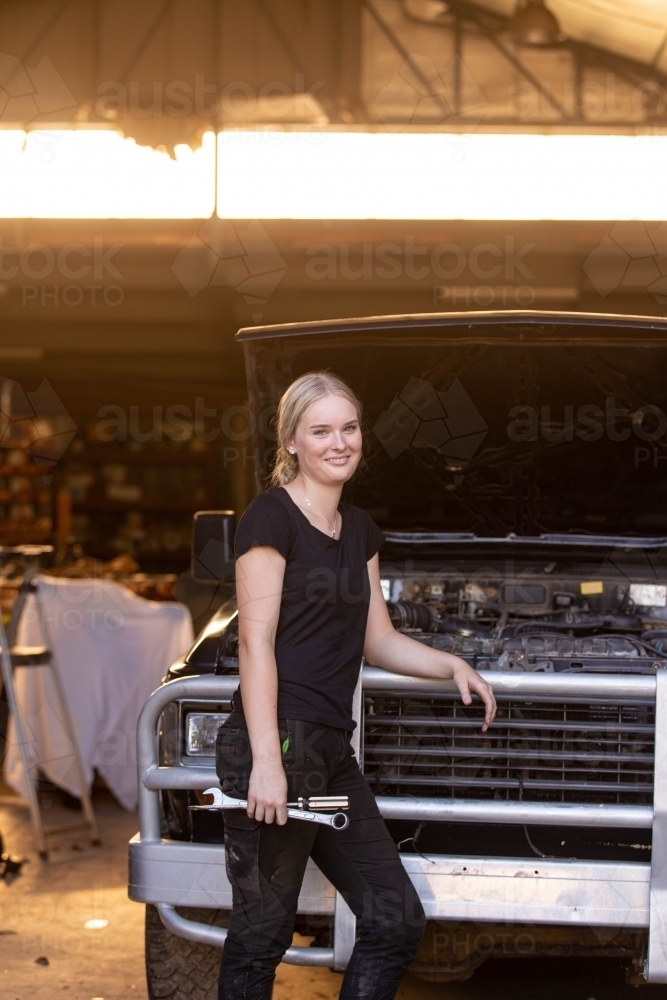 Image of Young female aussie mechanic holding tools and leaning on a ...