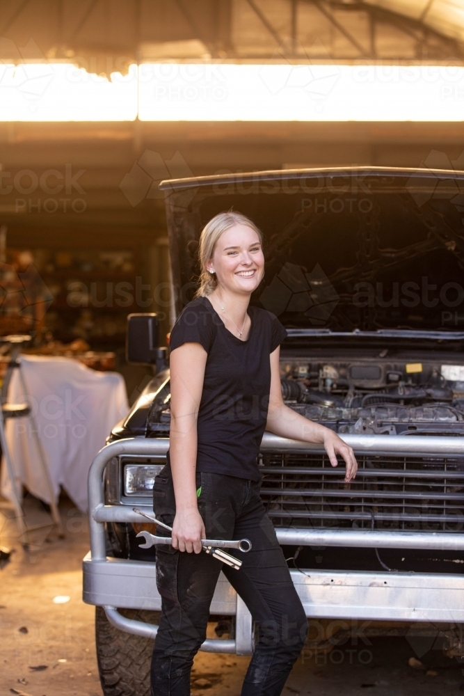 Image of Young female aussie mechanic holding tools and leaning on a ...