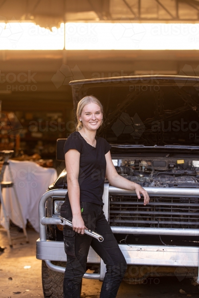 Image of Young female aussie mechanic leaning on a car in need of ...