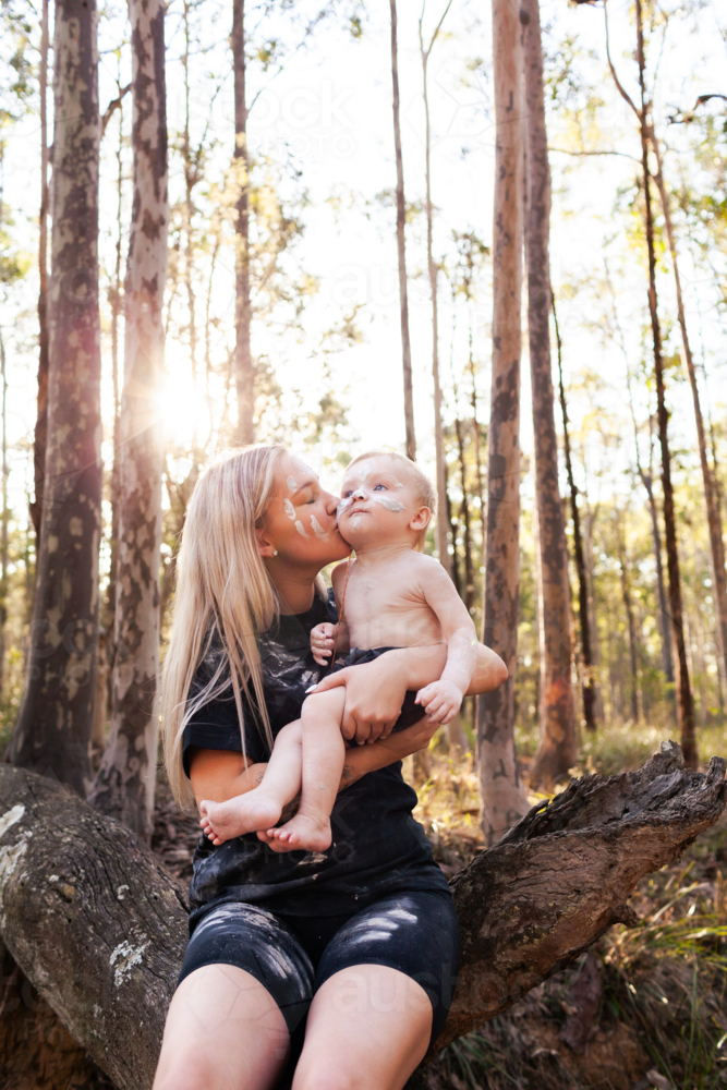Image of Young First Nations Australian woman kissing little child in sunlit National Park ...