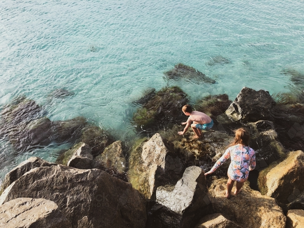 Image of Young girl and boy exploring rocks next to ocean - Austockphoto