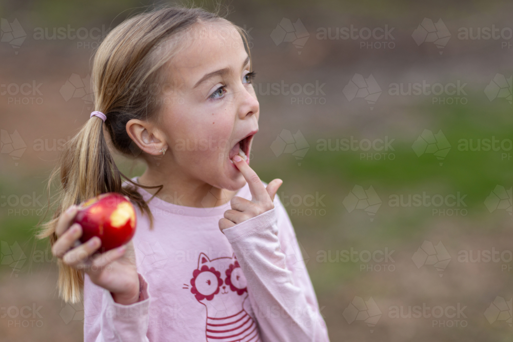 Image of Young girl eating an apple and pointing to her mouth ...
