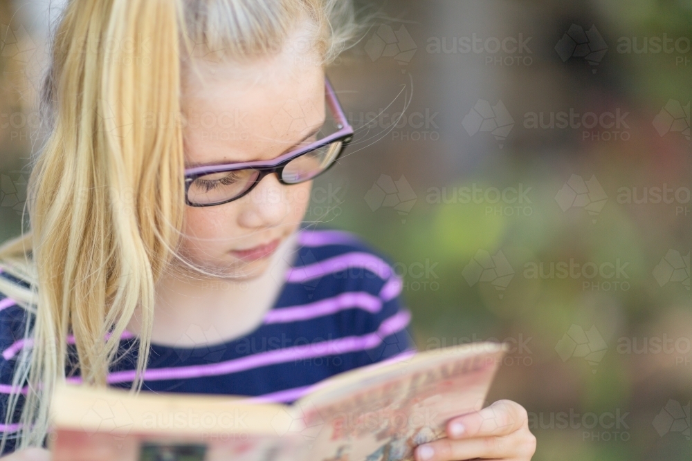 Image of Young girl engrossed in reading a book - Austockphoto