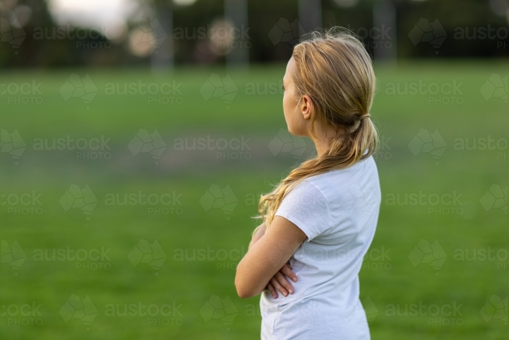 Image of young girl from behind looking away over green playing field ...