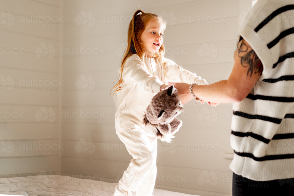 Image of Young girl jumping on the bed while holding mums hand ...