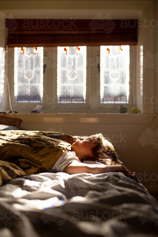 Image of Young girl lying on a bed with their arms stretched out above ...