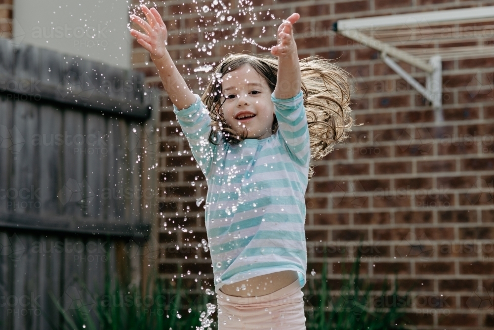 Image of Young girl playing in home backyard splashing water - Austockphoto