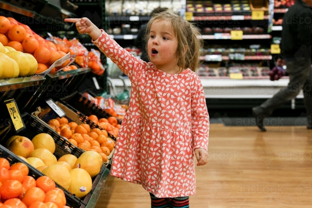 Image of Young Girl Pointing at Fruits in Supermarket - Austockphoto