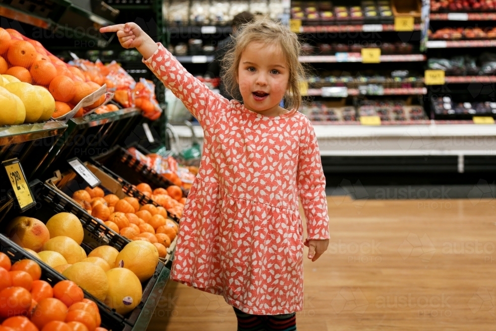 Image of Young Girl Pointing at Fruits in Supermarket Looking at Camera ...