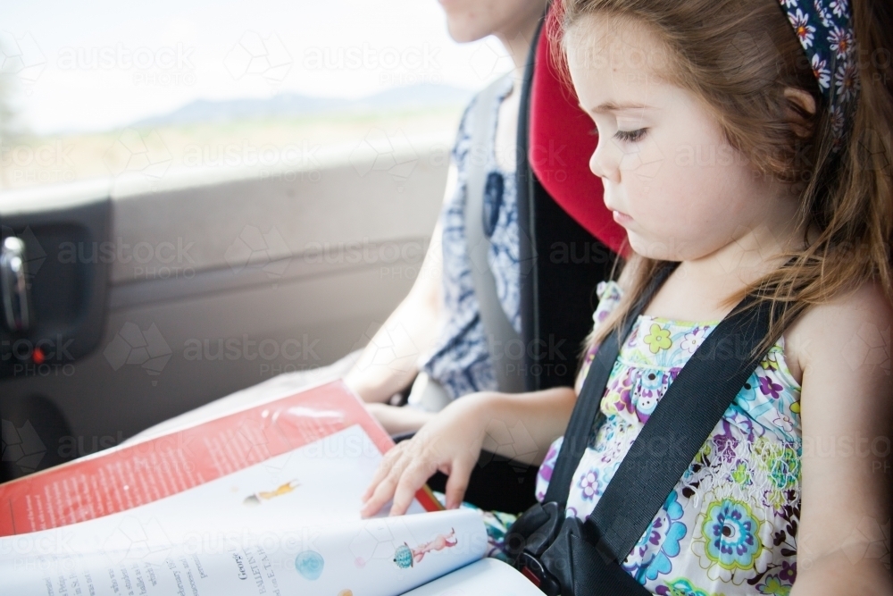 Image of Young girl reading a book in the car - Austockphoto