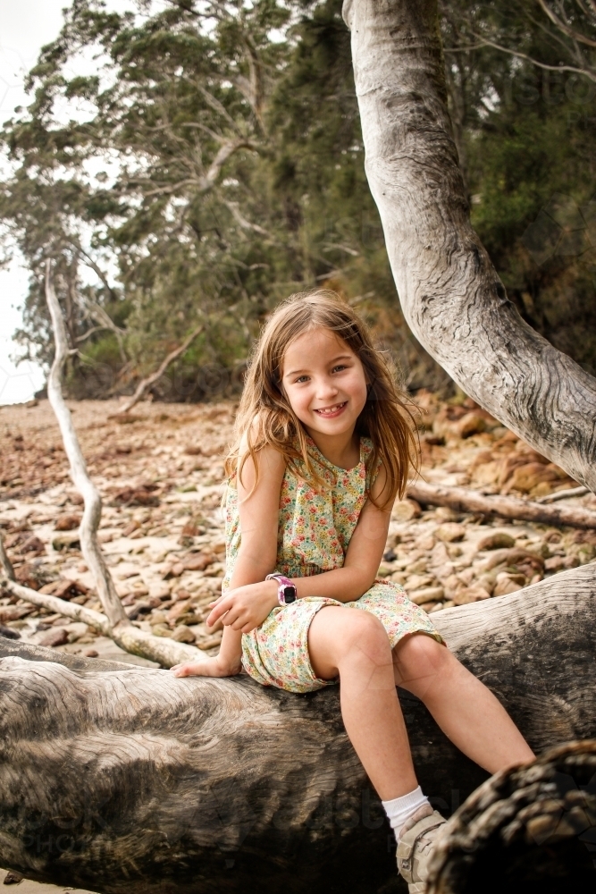 Image of Young girl sitting on a log between the bush and shore ...