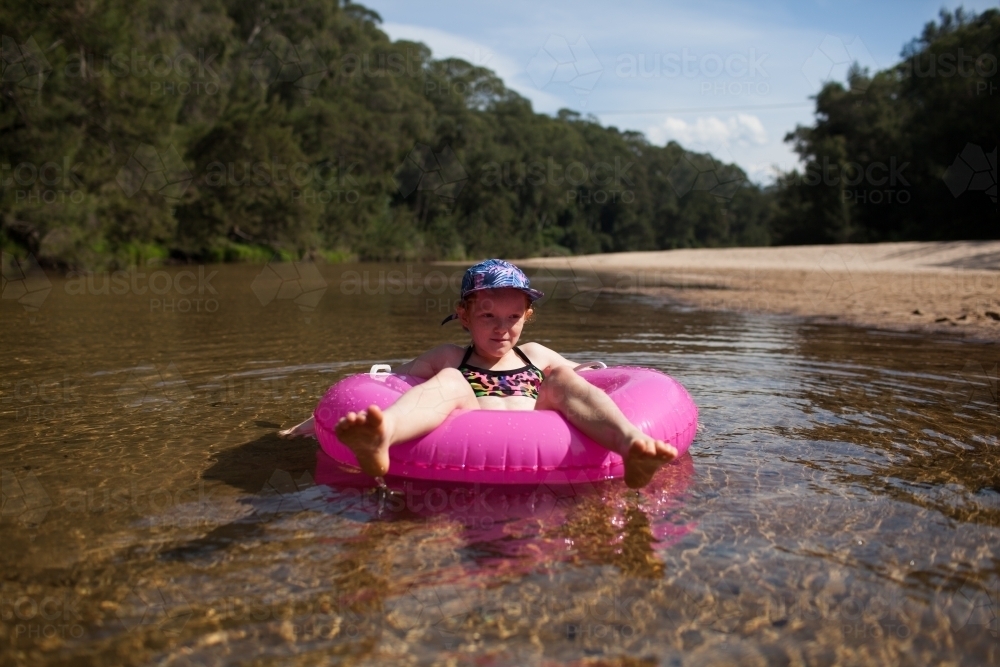 Image of Young girl sitting on a pink inflatable in a river - Austockphoto
