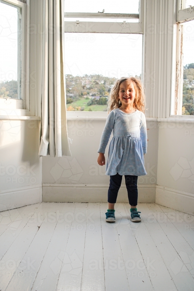 Image of Young girl standing in an empty room looking at camera smiling ...
