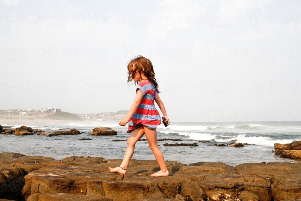 Image of Young girl walking over rocks by the ocean - Austockphoto
