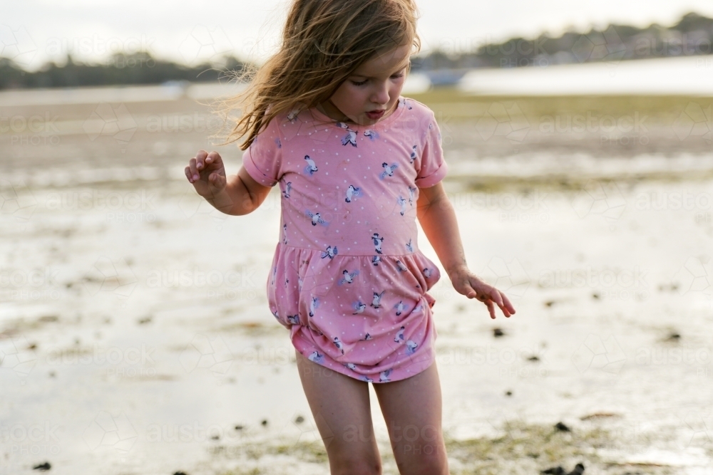 Image of Young girl wandering along and exploring the edge of the ocean ...