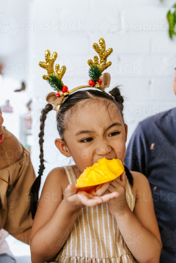 Image of Young girl with Christmas headdress enjoying ripe mango ...
