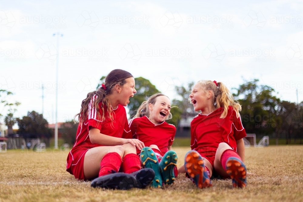 Image of Young girls wearing red soccer uniforms sitting on the field ...