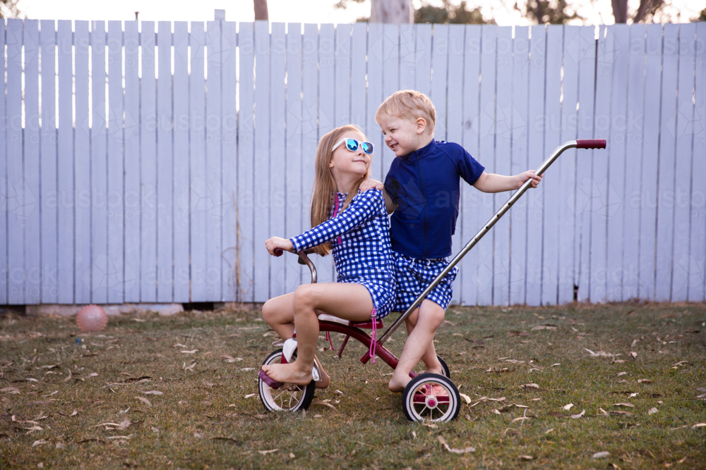 Image of young kids grinning at each other on the back of a trike ...