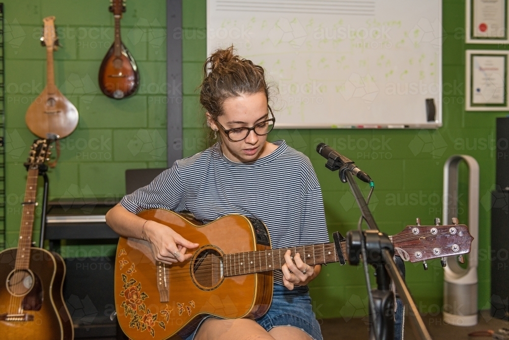 Image of Young lady playing guitar and singing - Austockphoto