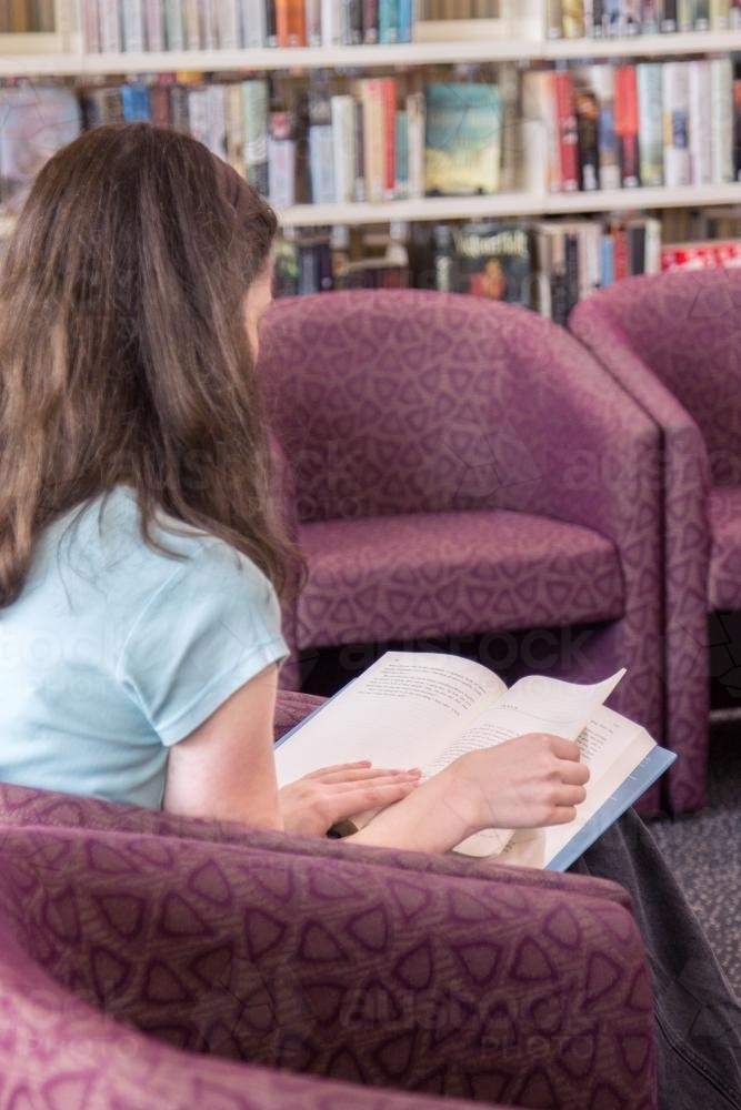 Image of Young lady sitting reading a book in the library - Austockphoto