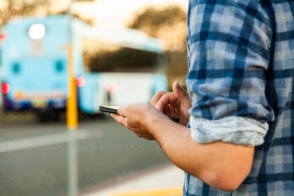 Image of Young male person waiting at bus stop checking times on mobile ...