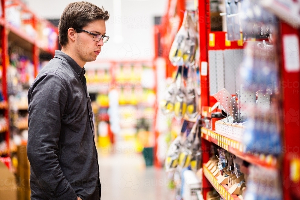 Image of Young man in hardware store looking at tools - Austockphoto