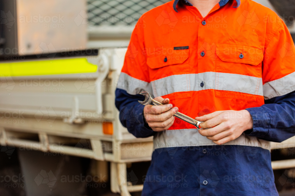 Image of Young man in workwear standing behind vehicle holding a ...