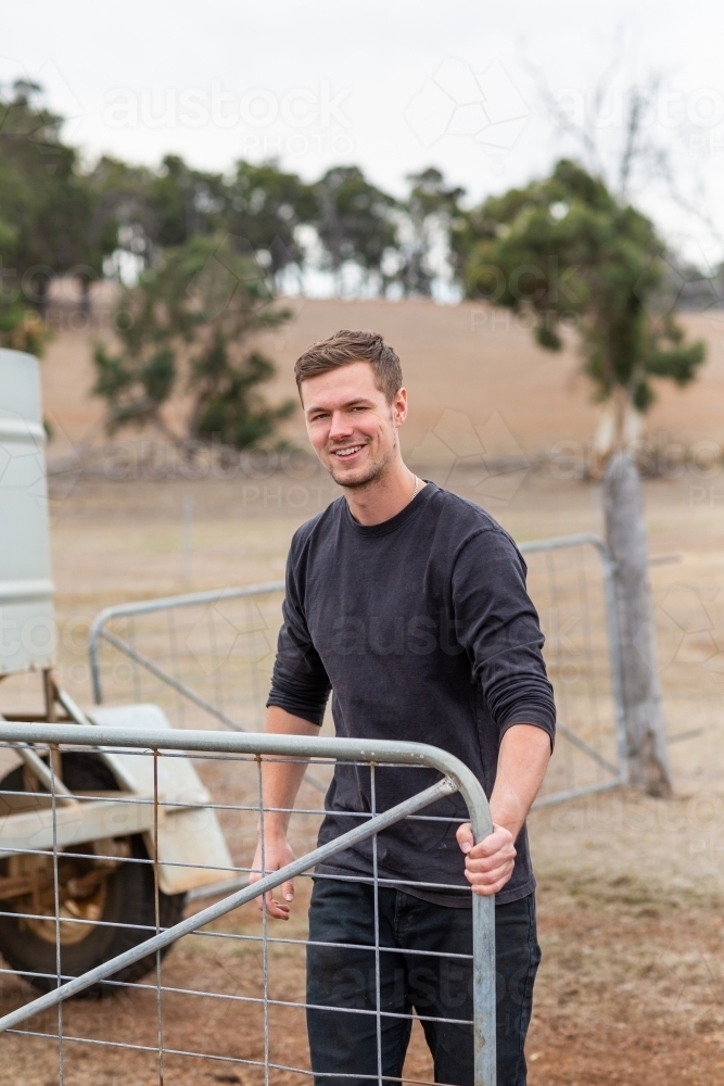 Image of Young man opening a gate on a country property - Austockphoto