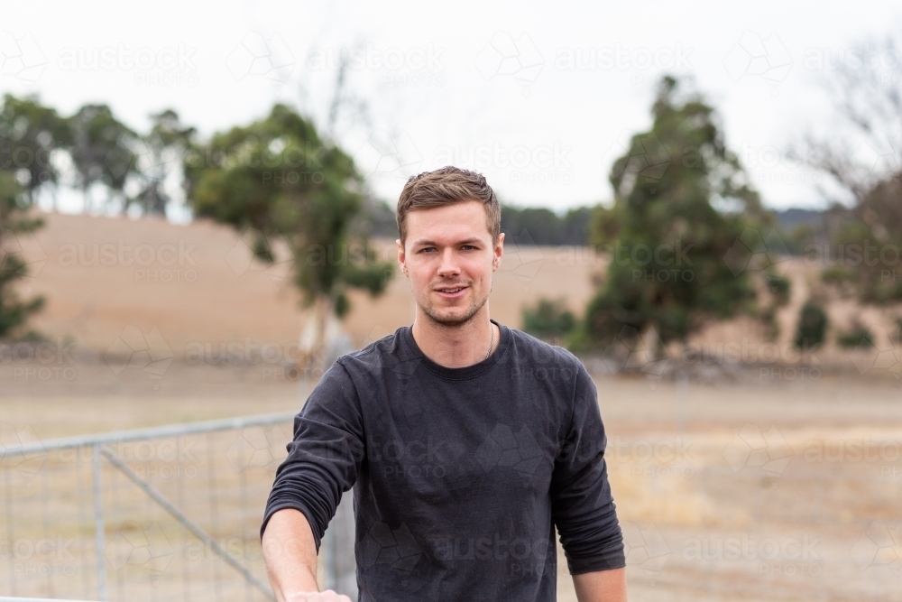 Image of Young man opening gate on country property - Austockphoto