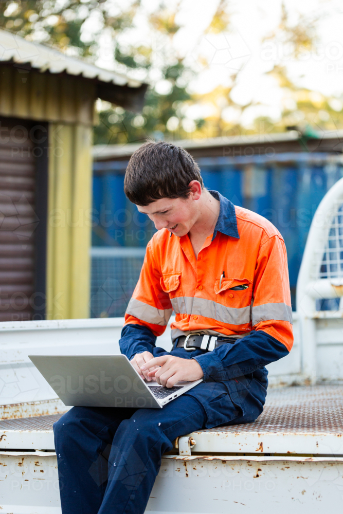 Image of Young man trainee tradie apprentice working on laptop in back ...