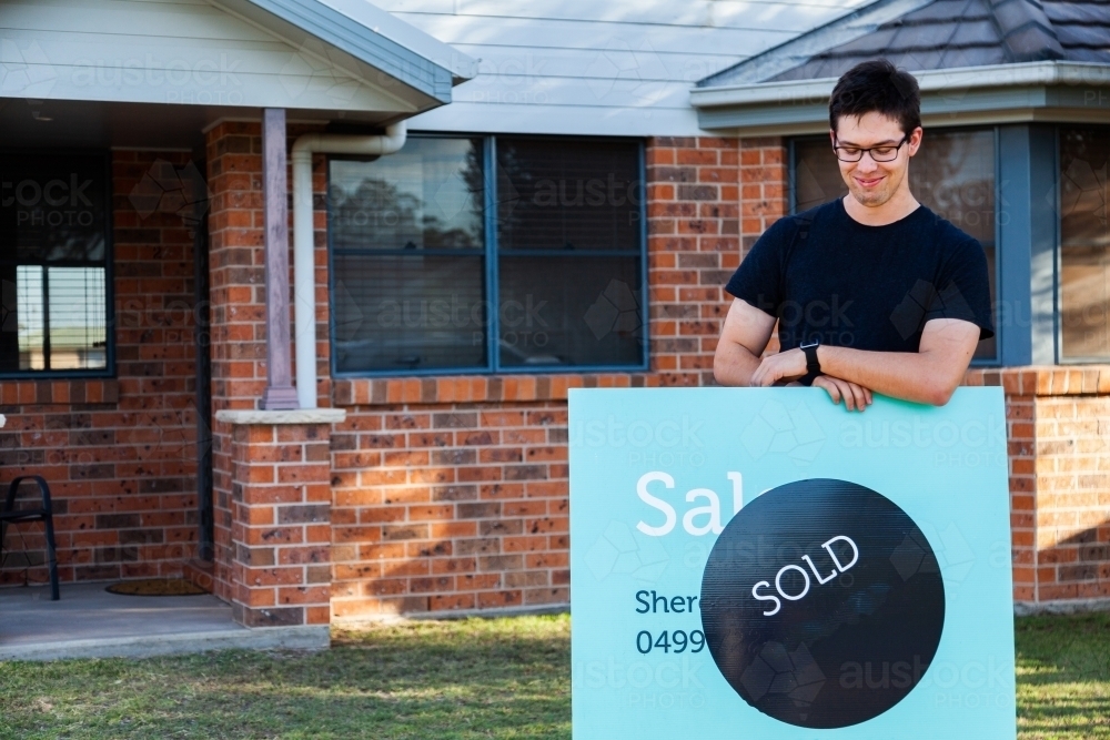 Image of Young man with sold sign and first home - Austockphoto