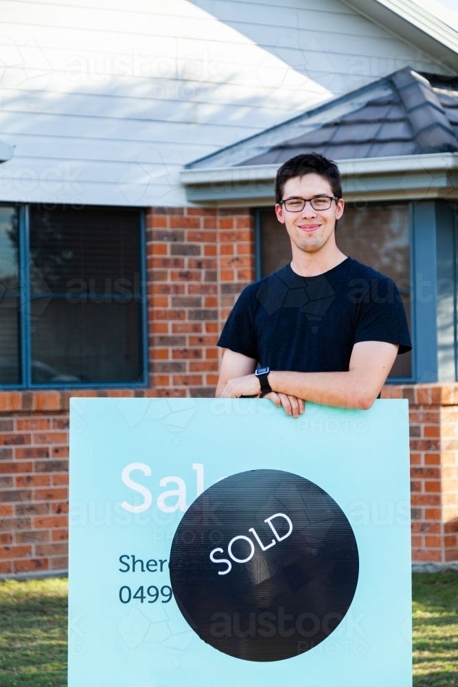 Image of Young man with sold sign and first home - Austockphoto