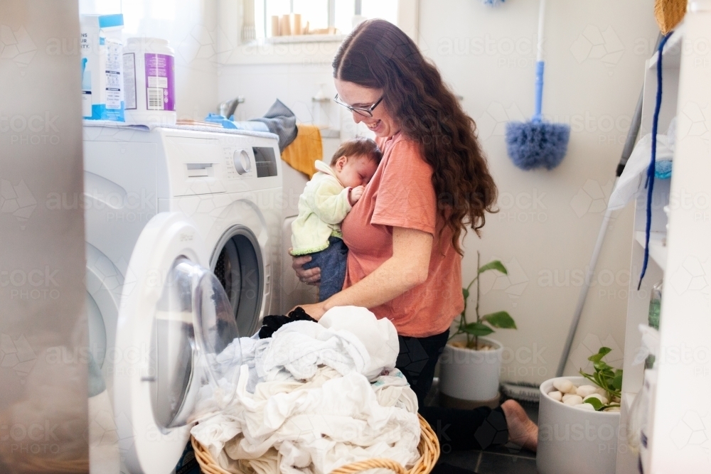 Image of Young mum taking wet clean clothes out of washing machine ...