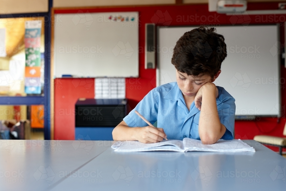 Image of Young school boy working on homework in classroom - Austockphoto