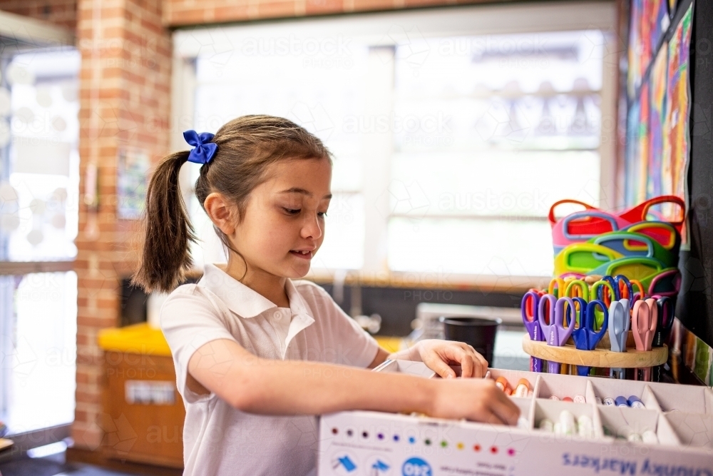 Image of Young Schoolgirl Packing Away art supplies in a Classroom ...