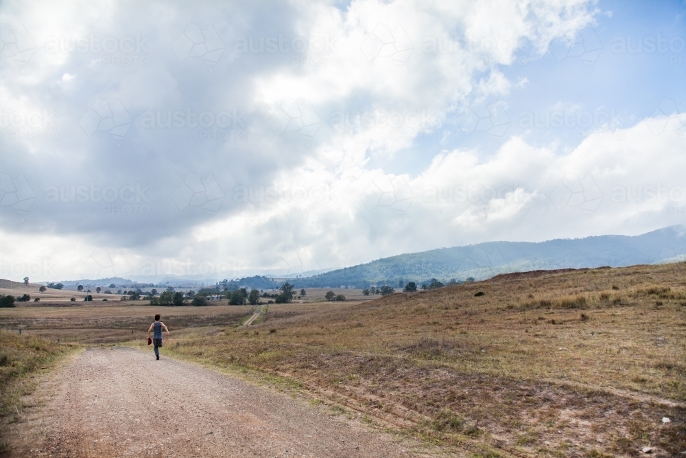 Image of Young teen running down driveway in dry paddocks - Austockphoto